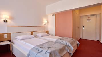 Quarto de hotel com duas camas, uma mesa de cabeceira e uma porta com uma placa.