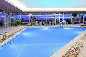 Piscina interior com água cristalina, rodeada por espreguiçadeiras e um deck revestido de azulejos.