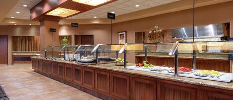 Uma área de buffet com várias estações de comida, incluindo buffet quente e uma estação de aveia.