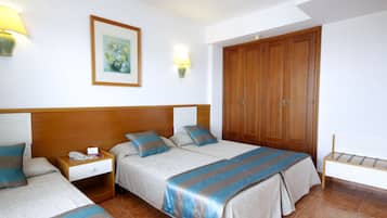 Quarto de hotel com duas camas, guarda-roupa de madeira, mesa de cabeceira com luminária e um quadro na parede.