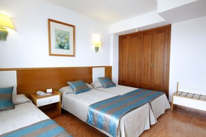 Quarto de hotel com duas camas, guarda-roupa de madeira, mesa de cabeceira com luminária e um quadro na parede.