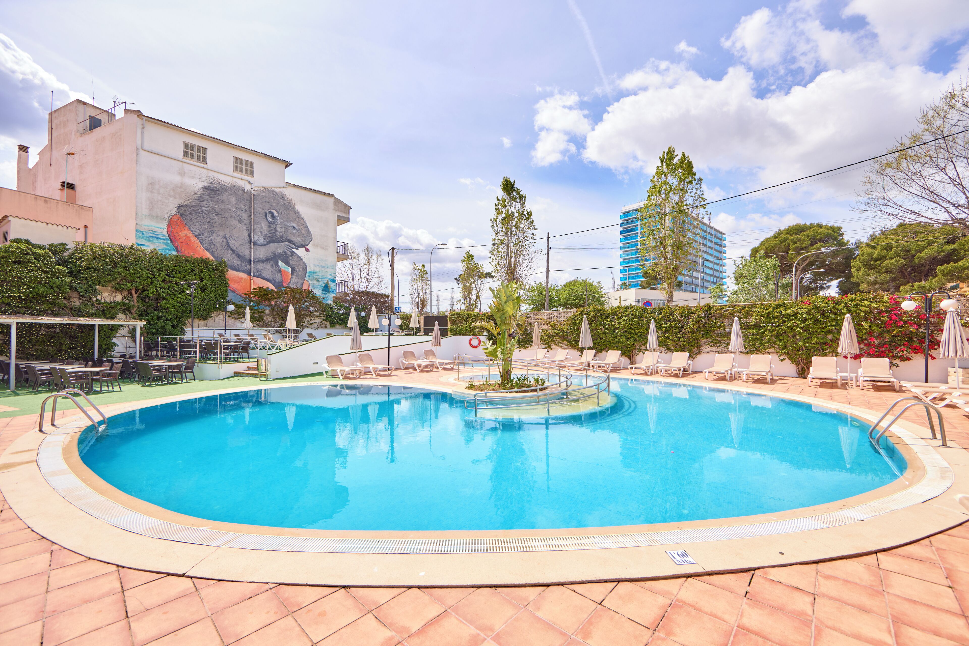 Piscina com espreguiçadeiras e um mural no prédio vizinho.