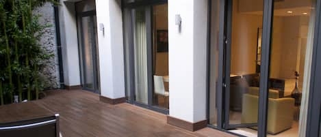 Quarto de hotel moderno com porta de vidro deslizante que dá para uma sala de estar, um deck de madeira e uma pequena área de estar ao ar livre.