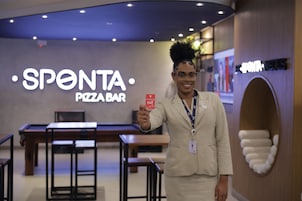Uma pessoa segurando um cartão vermelho em frente à placa do Sponta Pizza Bar.