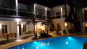 Um edifício de dois andares com piscina, área de estar externa e uma palmeira.