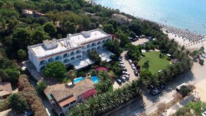 Vista aérea de um hotel à beira-mar com piscina, acesso à praia e vegetação exuberante.