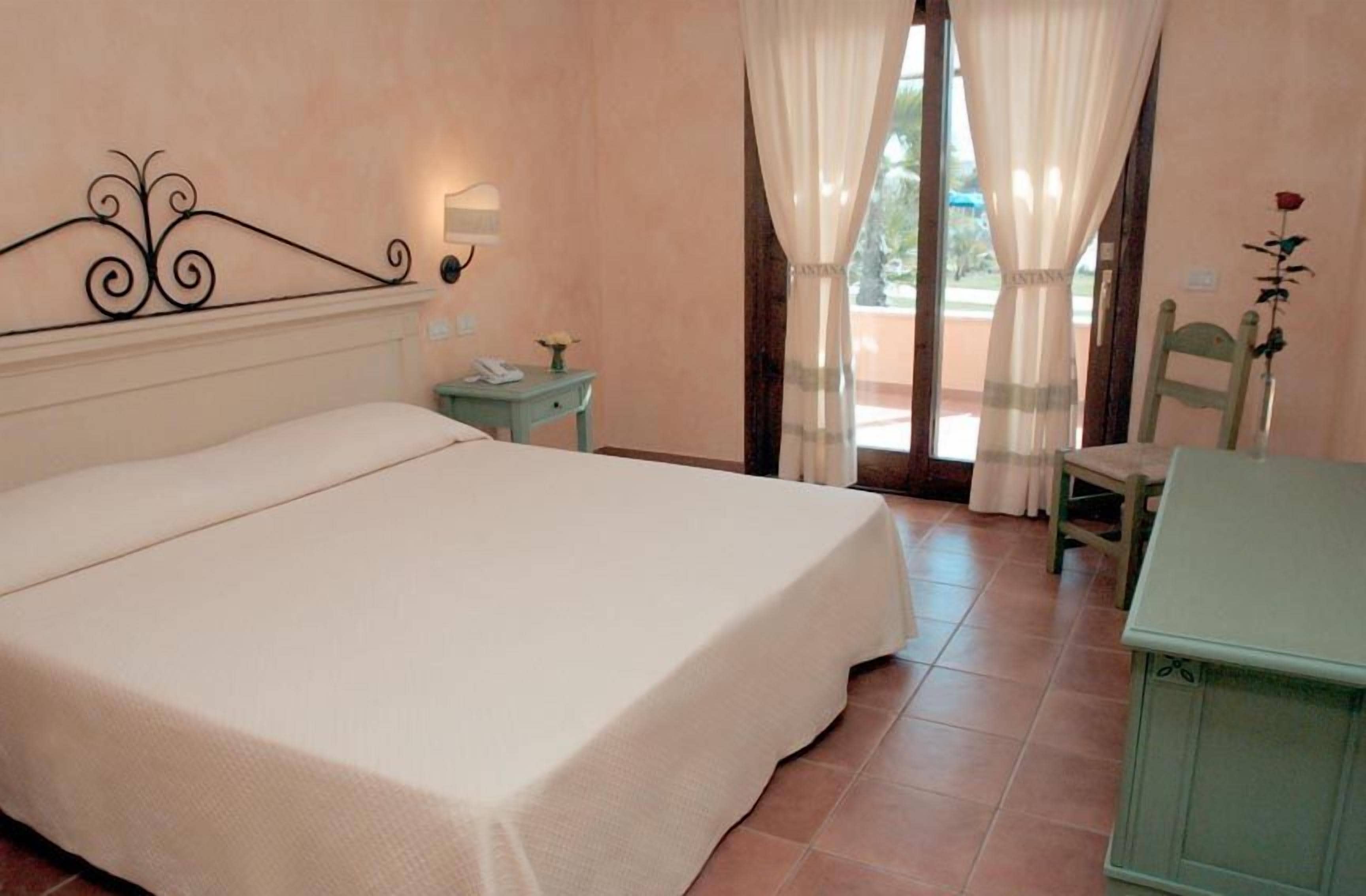 Quarto bem arrumado com cama, mesa de cabeceira, cadeira e vista para o exterior pela janela.