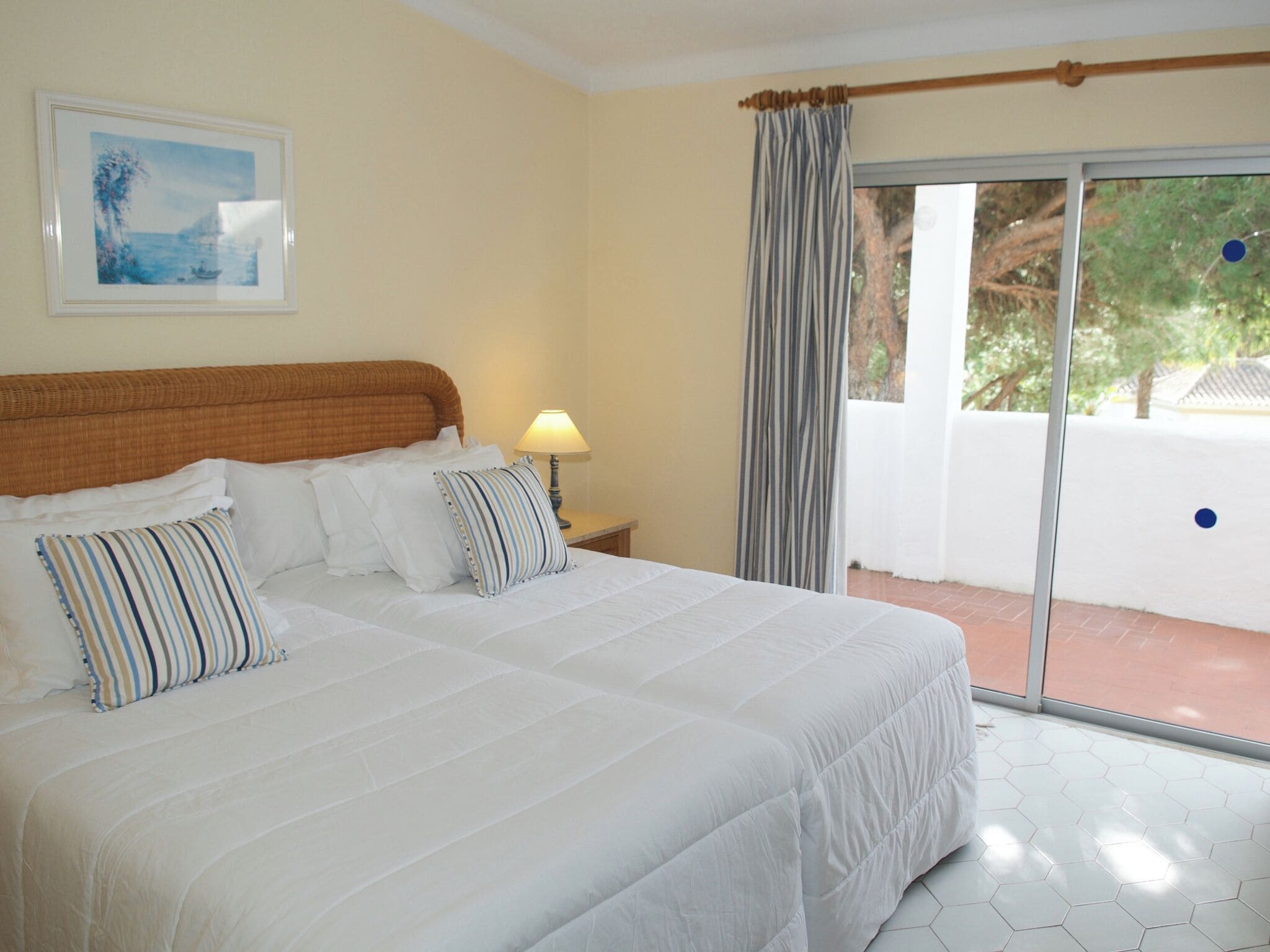 Quarto de hotel com uma cama grande, uma mesa de cabeceira, uma luminária, uma janela com cortinas e um quadro na parede.