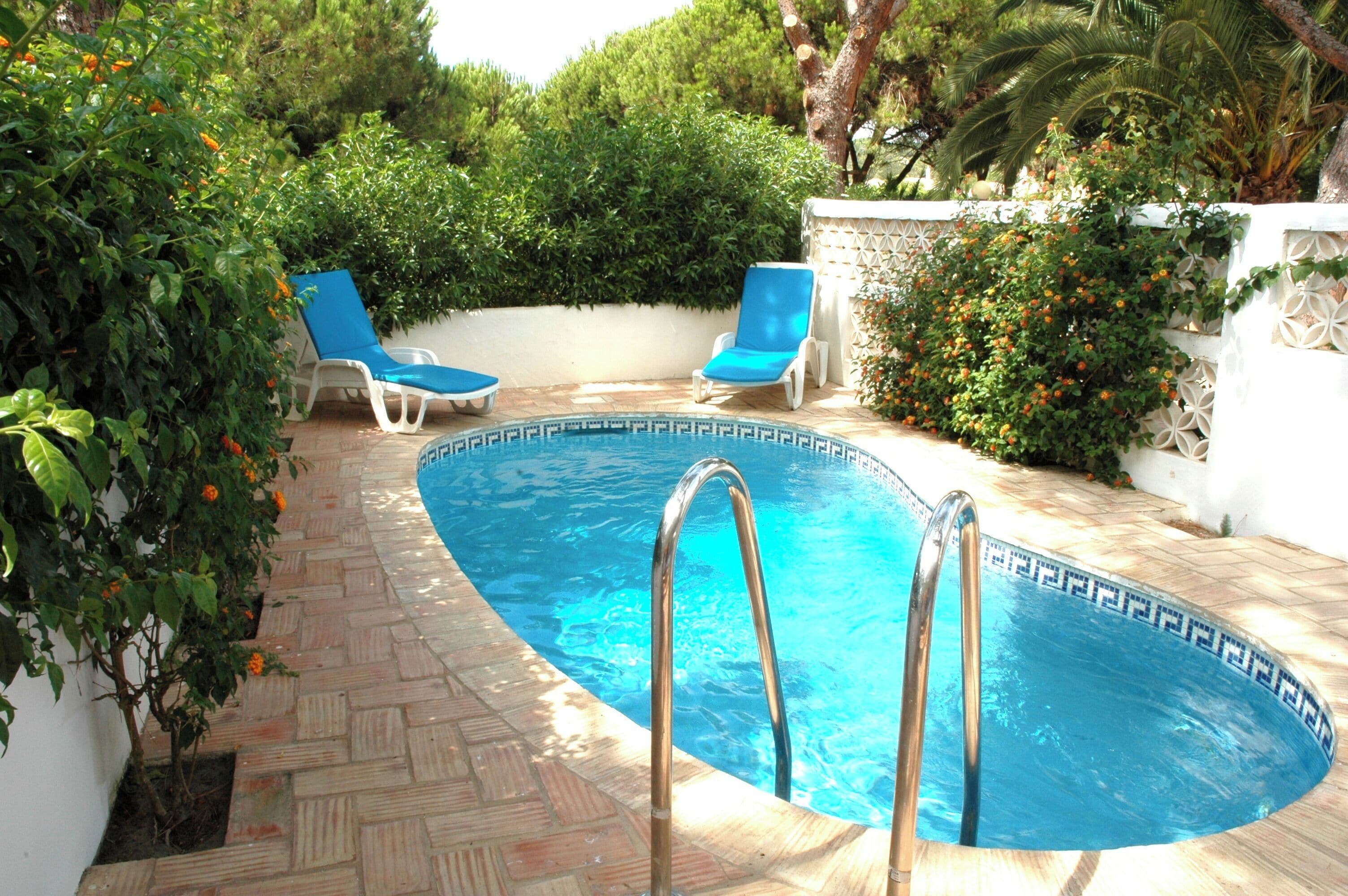 Piscina com duas cadeiras de descanso azuis e uma escada de metal.
