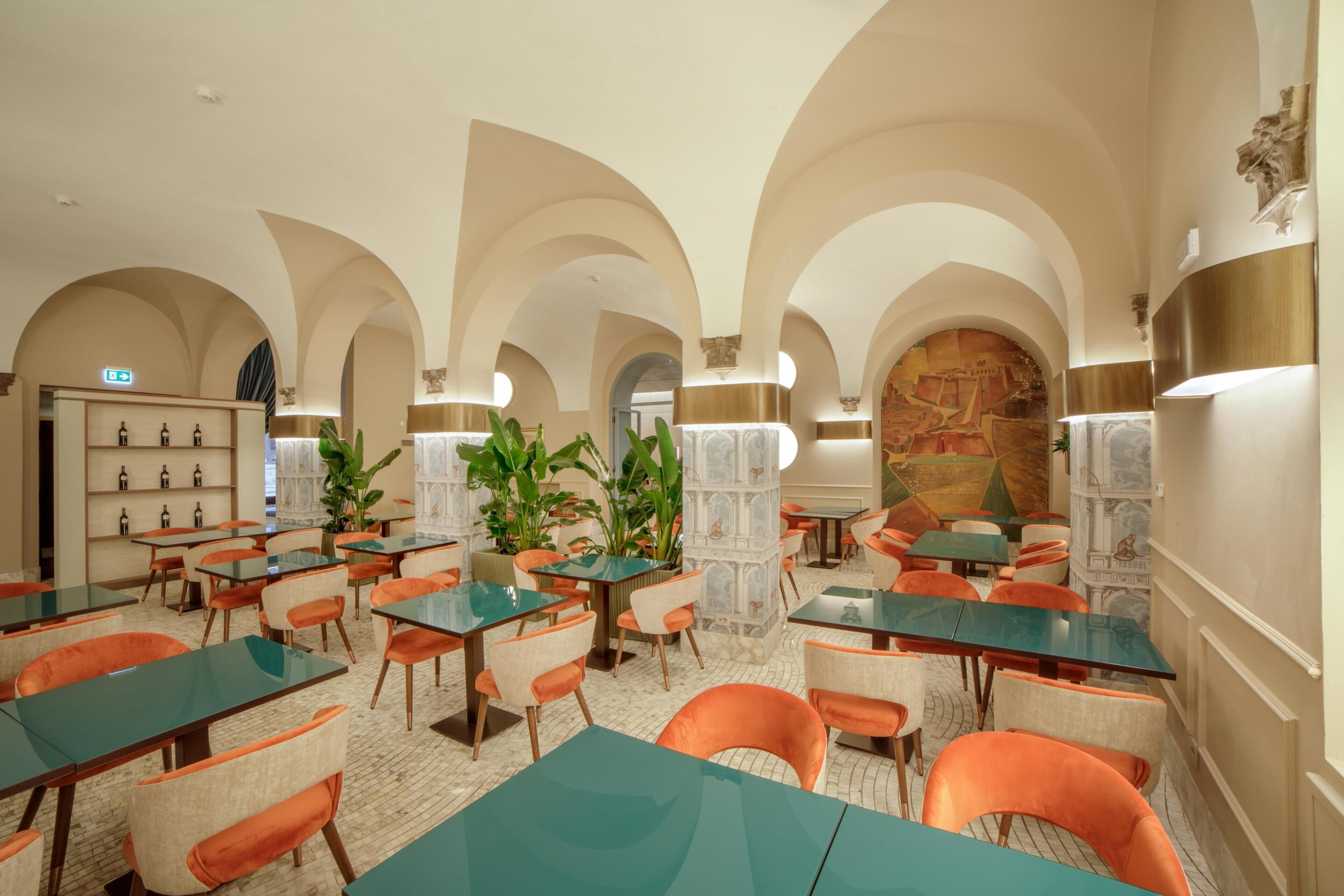 Um restaurante com várias mesas e cadeiras, teto abobadado e uma parede com um mural.