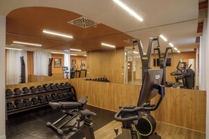 Academia com equipamentos de ginástica, espelho e suporte de halteres.