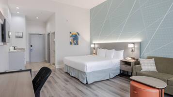 Quarto de hotel com cama, mesa de cabeceira, abajur e um pequeno banquinho laranja.