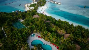 Vista aérea de um resort com piscina, praia e bangalôs sobre a água.