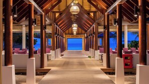 Uma galeria coberta com acesso à praia, com pilares de madeira, áreas de estar e luzes penduradas.