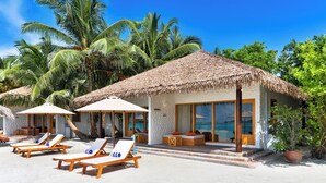 Um resort à beira-mar com villas de telhado de palha, espreguiçadeiras e palmeiras.