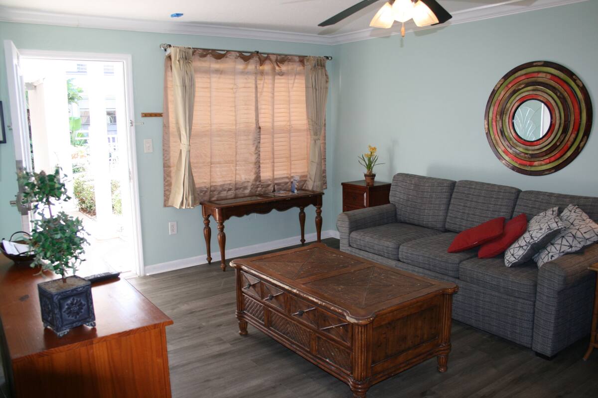 Uma sala de estar com um sofá, uma mesa de centro de madeira e um espelho decorativo na parede.