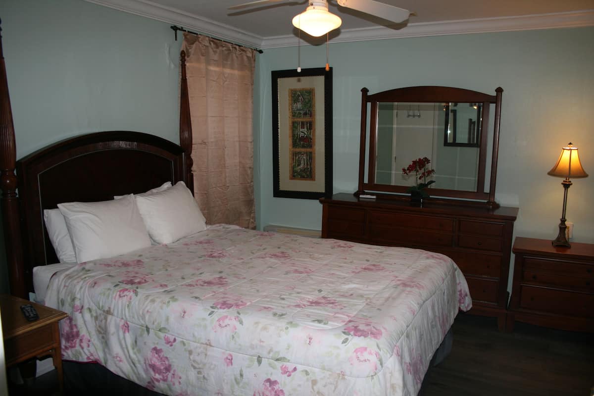 Quarto com cama, penteadeira, espelho e ventoinha no teto.
