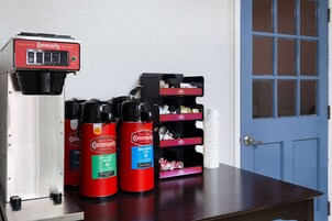 Uma estação de café com uma máquina de café e três dosadores vermelhos de café com a etiqueta 'Community Coffee'.