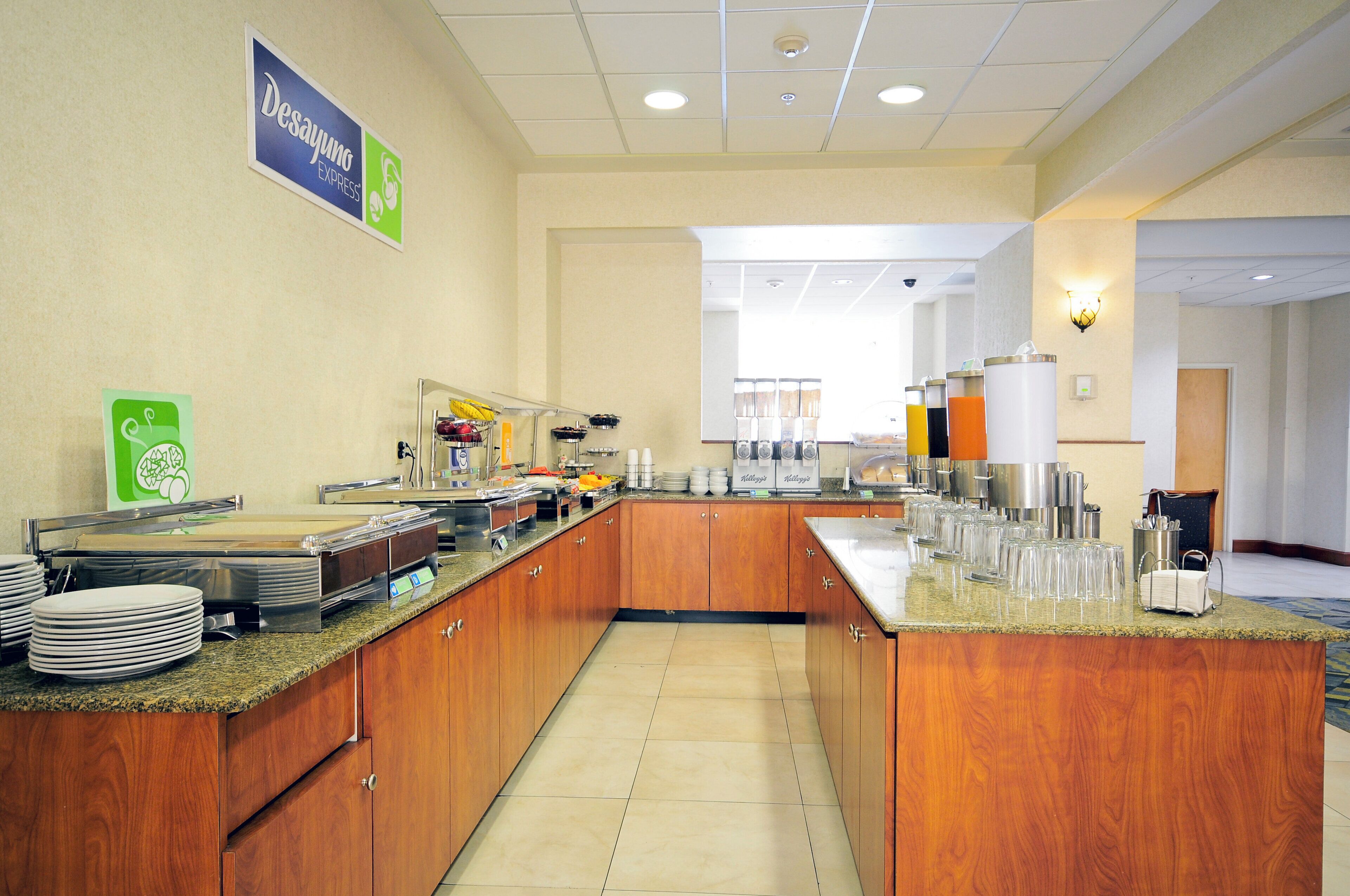 Espaço de café da manhã de hotel com buffet, incluindo uma placa para Desayuno Express, uma estação de café e diversos recipientes com alimentos.