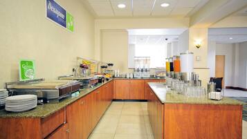 Espaço de café da manhã de hotel com buffet, incluindo uma placa para Desayuno Express, uma estação de café e diversos recipientes com alimentos.