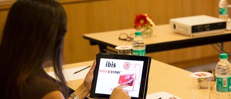 Uma pessoa usando um tablet com o aplicativo ibis web corner, uma garrafa de água, um copo e um projetor sobre uma mesa em um quarto com painéis de madeira.