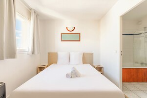 Quarto de hotel com cama grande, mesa de cabeceira, quadro emoldurado e área de chuveiro.