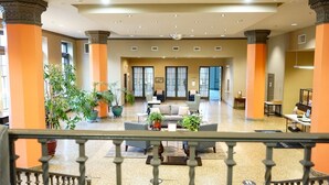 Um hall amplo com área de estar central, grandes janelas e plantas em vasos.
