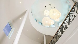 Um interior moderno com uma clarabóia circular central, uma escada com guarda-corpo de metal e iluminação embutida no teto.