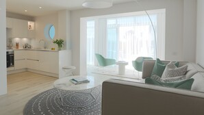 Uma sala de estar moderna com sofá, mesa de centro e área de jantar, com cozinha ao fundo.