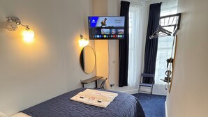 Quarto de hotel com uma cama, televisão na parede, espelho e janela com cortinas.