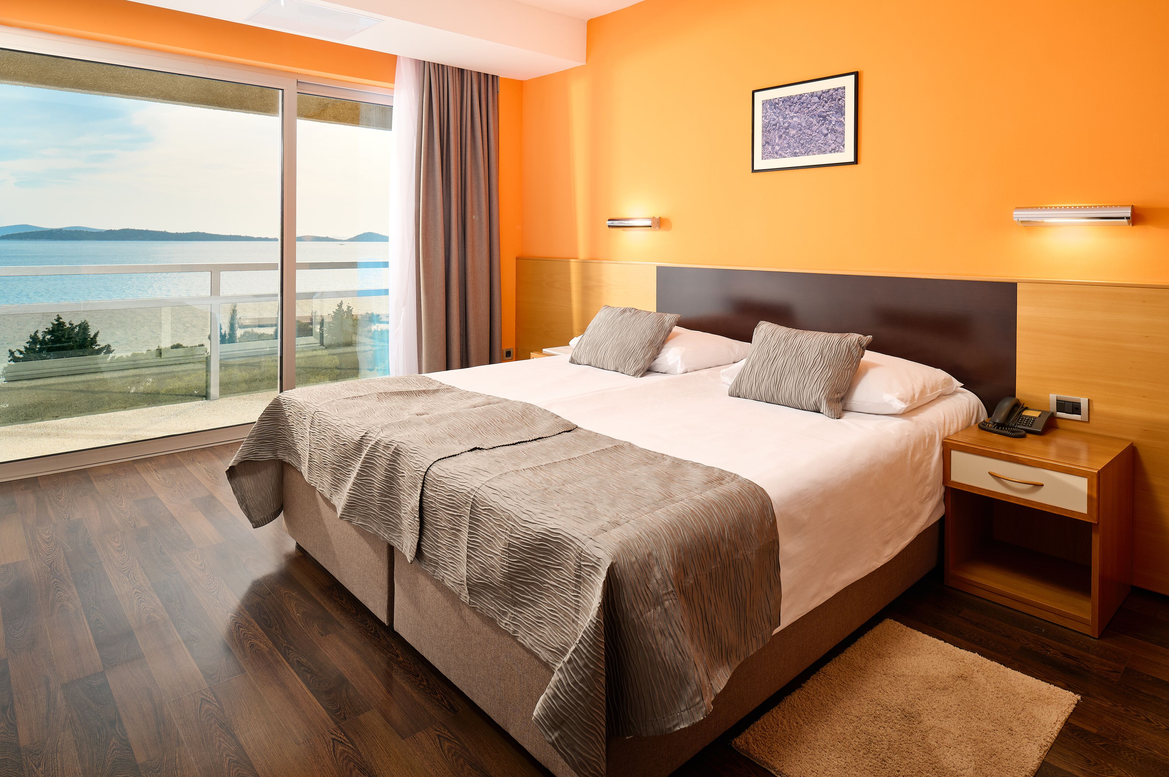 Quarto de hotel com uma cama grande, uma mesinha de cabeceira, uma janela com vista para o mar e um quadro na parede.