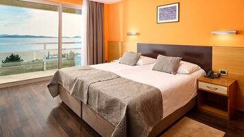 Quarto de hotel com uma cama grande, uma mesinha de cabeceira, uma janela com vista para o mar e um quadro na parede.