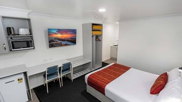 Quarto de hotel com cama, escrivaninha, cadeira, micro-ondas, mini-geladeira, quadro e guarda-roupa.
