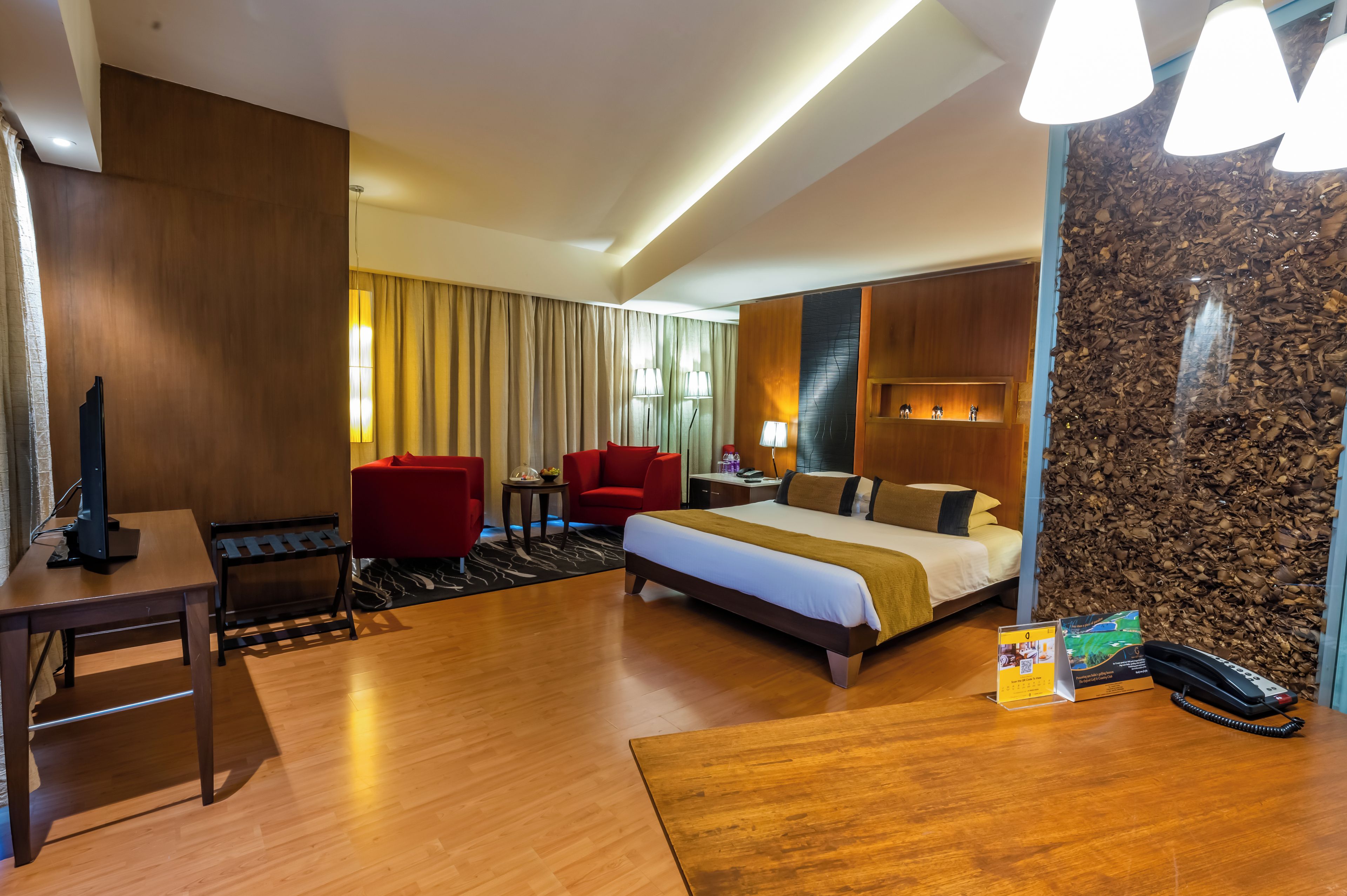 Quarto de hotel com cama, escrivaninha, cadeira, televisão e painel decorativo na parede.
