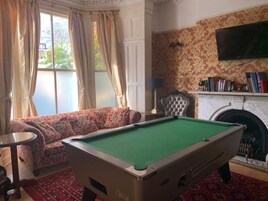 Uma mesa de bilhar em uma sala com sofá, lareira e estante de livros.