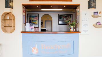 Balcão de recepção com um aviso de 'Welcome', um relógio e a placa 'Beachcroft Hotel on the Beach'.
