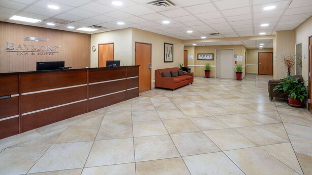 Uma área de recepção com balcão de madeira, sofá vermelho, plantas em vasos e placa da Baymont Inn & Suites.