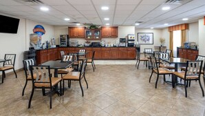 Uma área de café do manhã espaçosa, com armários de madeira, bancada com diversos eletrodomésticos e várias mesas e cadeiras.