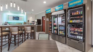 Um saguão de hotel com área de recepção, bar e área de estar. Há dois dispensadores de bebidas identificados como “REFRESH” e “HYDRATE”.