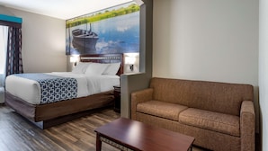 Quarto de hotel com uma cama, um sofá, uma mesinha e um quadro de um barco em um rio.