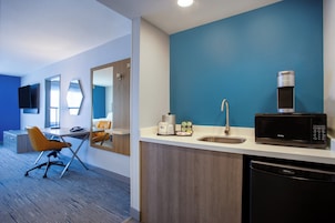 Quarto de hotel moderno com cozinha compacta, máquina de café, micro-ondas e pia.