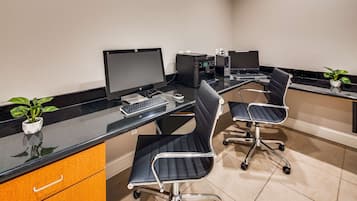 Um espaço de escritório moderno, com mesas, cadeiras, computadores e um vaso de planta.