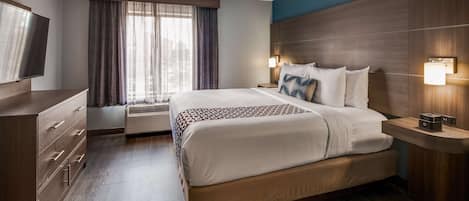 Quarto de hotel com cama, televisão, secretária com abajur e janela com cortinas.