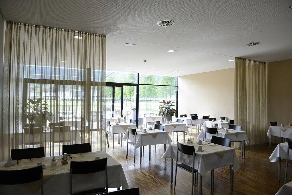 Uma sala de conferências com várias mesas e cadeiras, janelas amplas e teto com iluminação embutida.