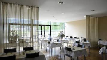 Uma sala de conferências com várias mesas e cadeiras, janelas amplas e teto com iluminação embutida.
