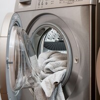 Máquina de lavar roupa com abertura frontal, porta transparente e painel de controle com diversas configurações, com uma toalha no interior.