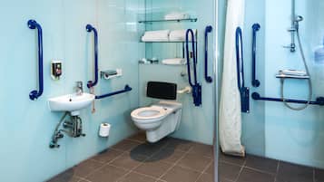 Uma casa de banho moderna com sanita, lavatório e chuveiro. Possui barras de apoio e cabine de duche em vidro.