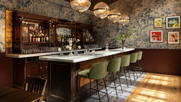 Uma área de bar com balcão de madeira, luminárias pendentes e um painel de parede com papel de parede floral.