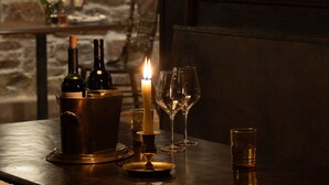 Uma mesa com velas, garrafas de vinho, copos e castiçais.