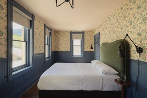 Quarto com uma cama grande, duas janelas, uma mesa de cabeceira e uma luminária.